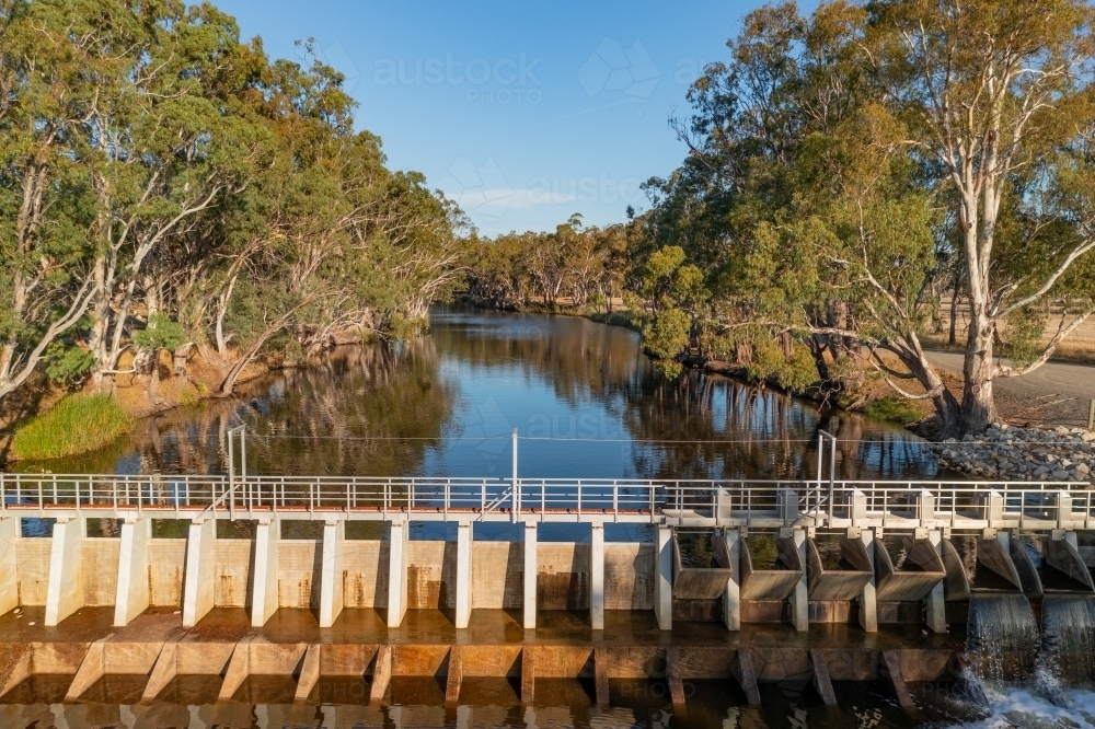 Image of Aerial view of a weir on a dirty brown river with gum trees on ...