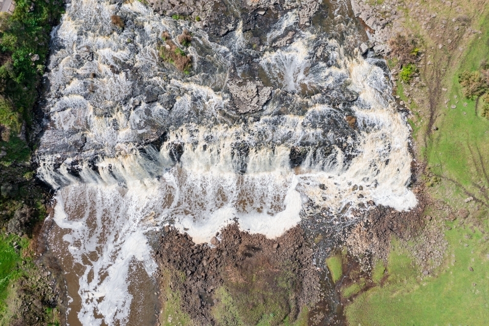 Image of Aerial view of a wide rocky waterfall tumbling into a green ...