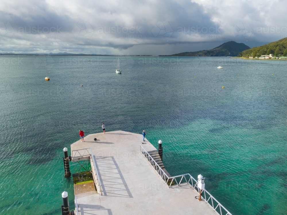 Image of Aerial view of fishermen on a concrete jetty over a calm bay ...