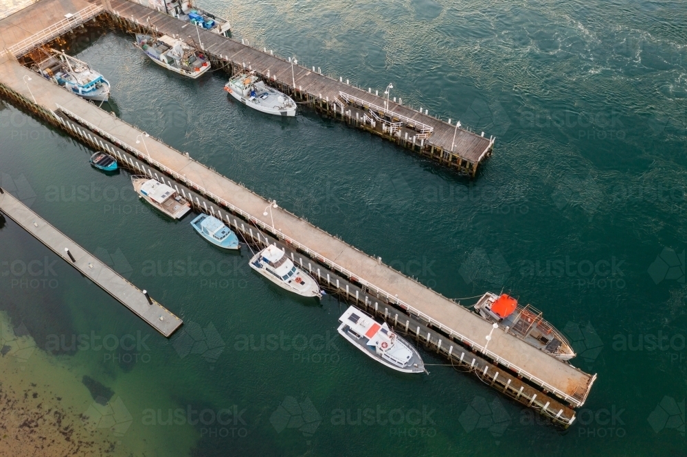 Image of Aerial view of fishing boats docked alongside a jettys over a ...
