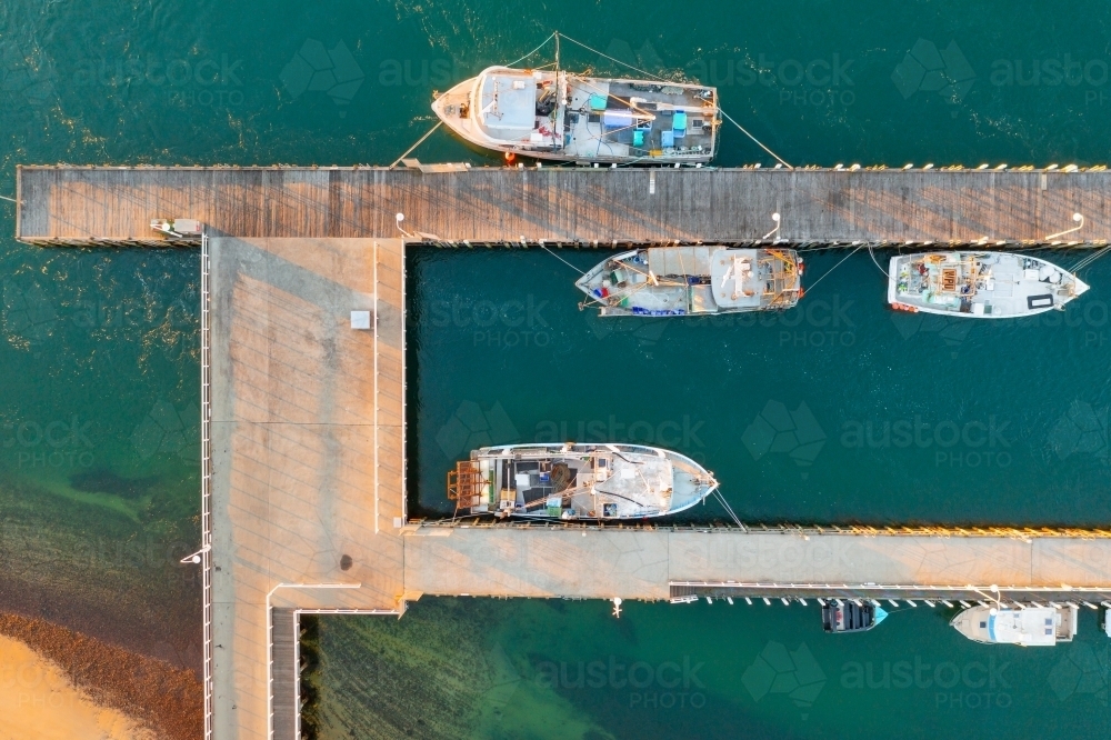 Image of Aerial view of fishing boats docked alongside a jettys over a ...