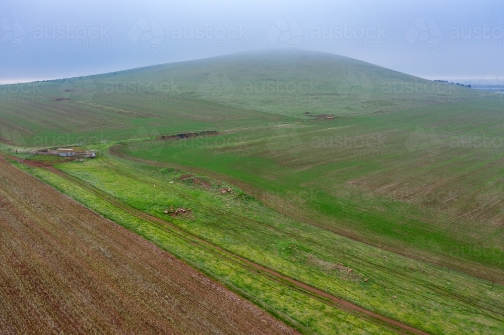 Image of Aerial view of fog over green farmland and a low rounded hill ...