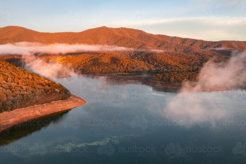 Image of Aerial view of fog patches lifting from a lake surrounded by ...
