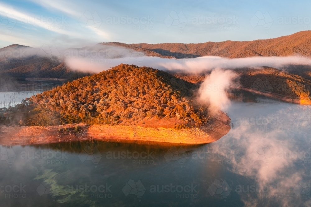Image of Aerial view of fog patches lifting from a lake surrounded by ...