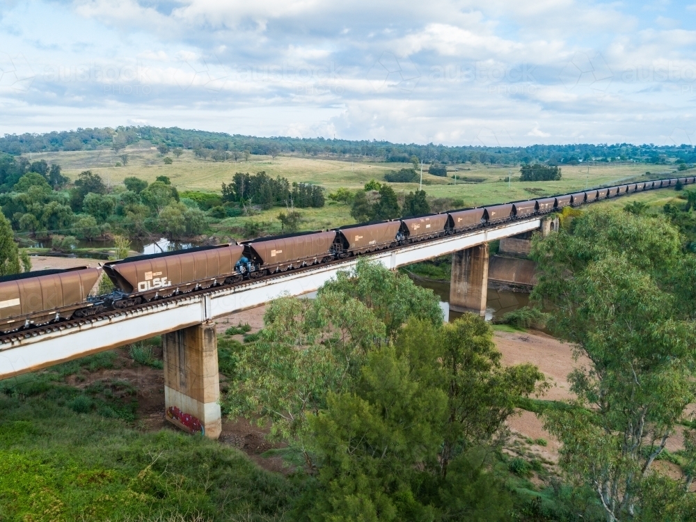 Image of aerial view of full coal train crossing bridge over river ...