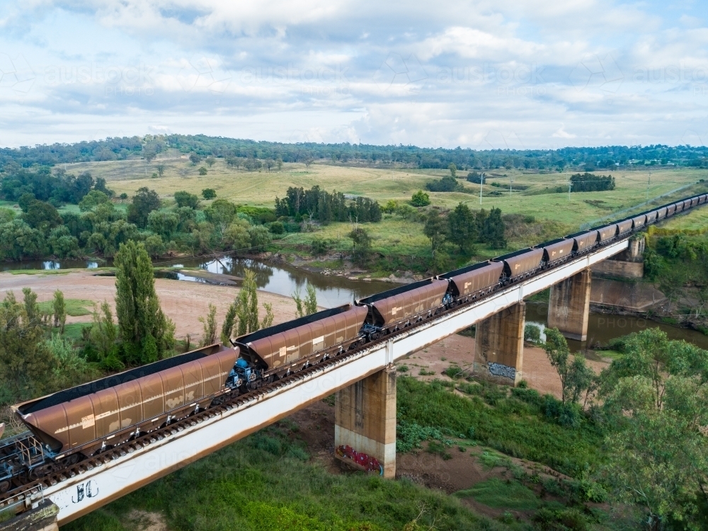 Image of aerial view of full coal train crossing bridge over river ...