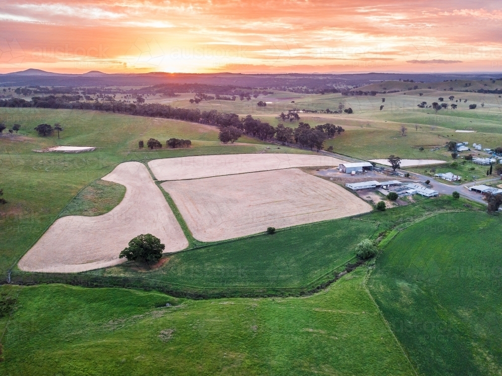 Image of Aerial view of ploughed paddocks near farm buildings at sunset ...
