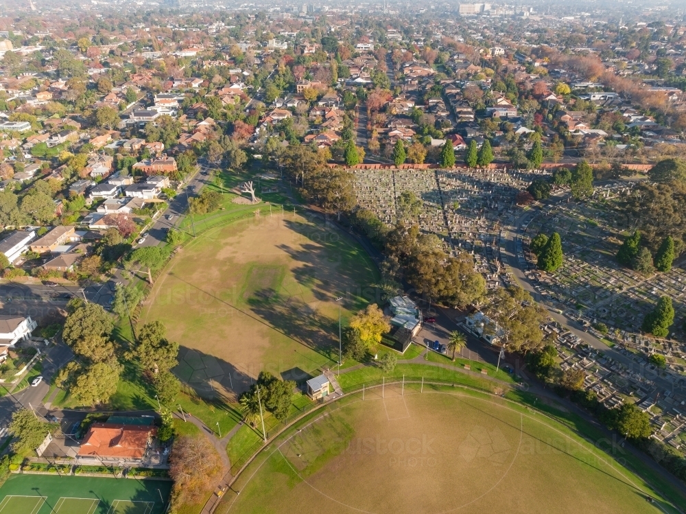 Image of Aerial view of sporting ovals alongside a suburban cemetery ...