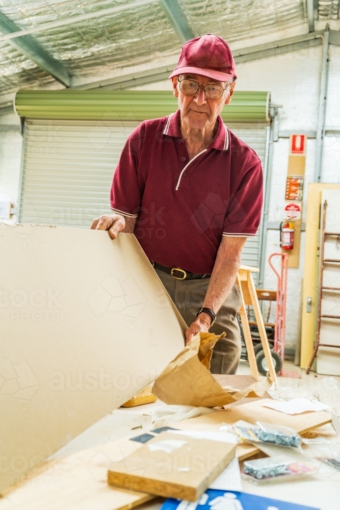 Image of An elderly handyman lifting a piece of timber in a Men's shed ...