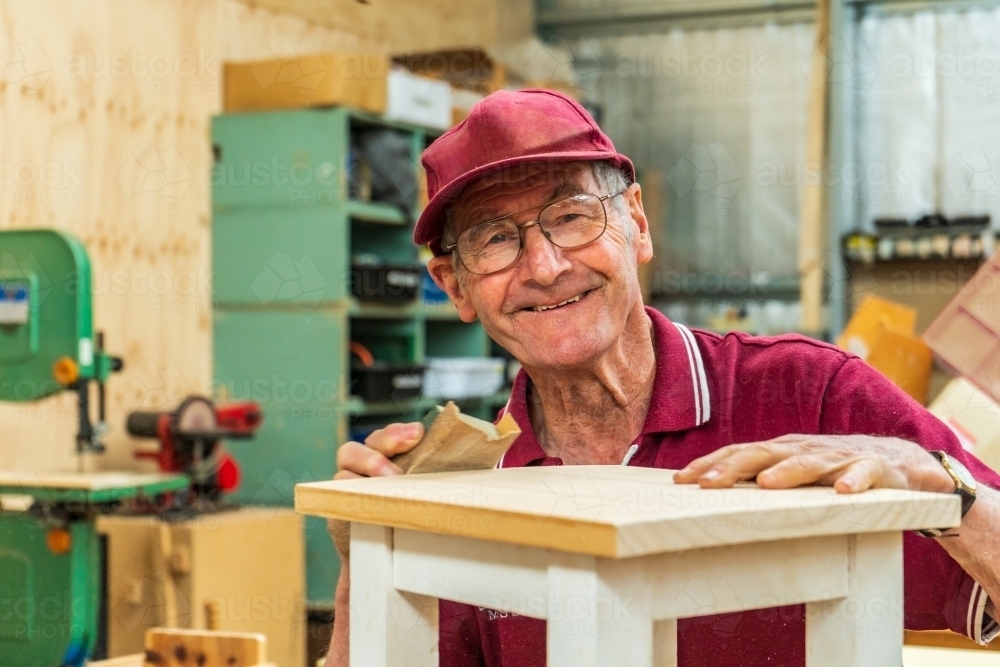 Image of An elderly handyman smiling over the top of a piece of ...