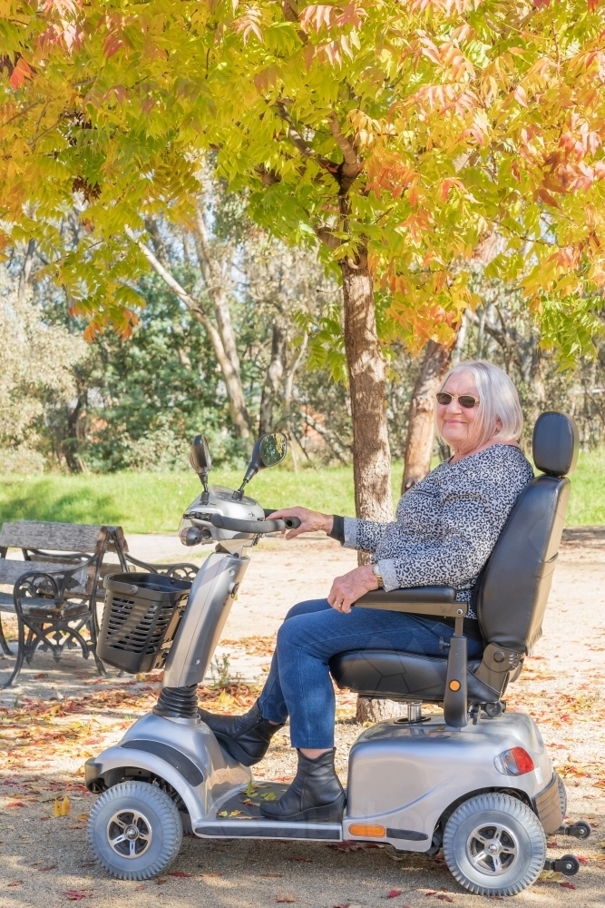 Image of An elderly woman in a mobility scooter under an autumn tree in ...
