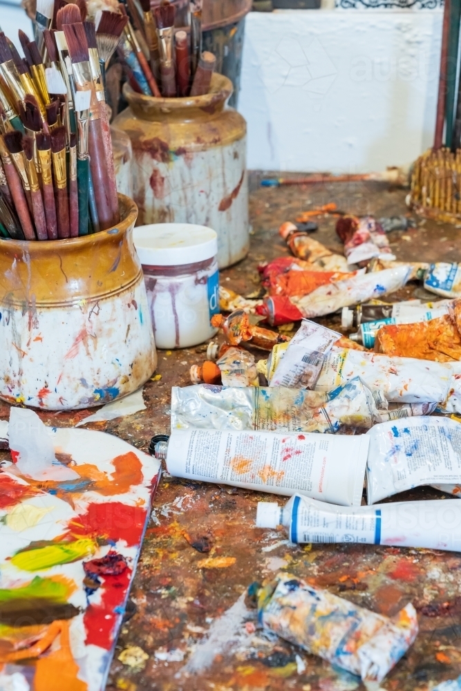 Image of An messy artist's table covered in colourful paint and brushes ...