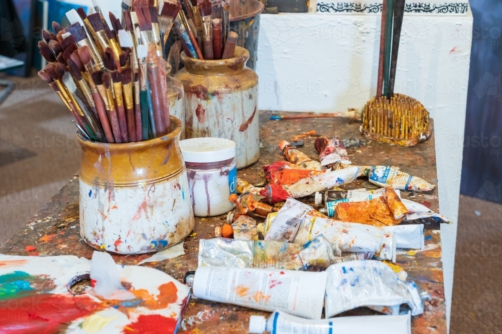 Image of An messy artist's table covered in colourful paint and brushes ...