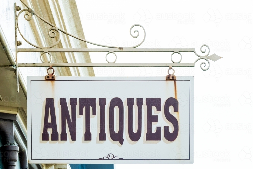 Image of An old world antiques sign hanging from a decorative metal ...
