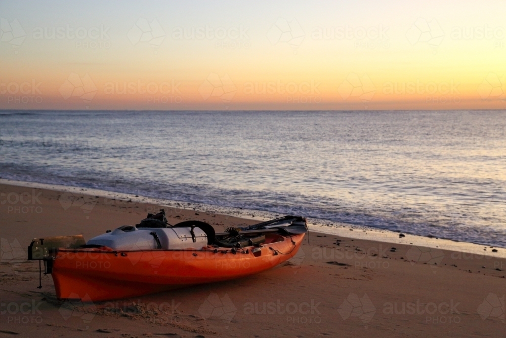 Image of An orange fishing kayak sitting on a beach at sunrise ...