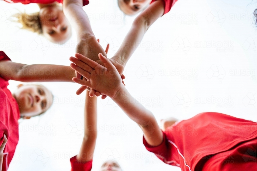 Image of An upward view of tween girls football team joining hands ...