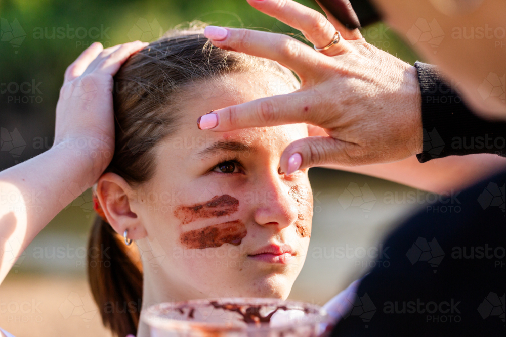 Image of Applying ochre face paint to aboriginal girls skin - Austockphoto