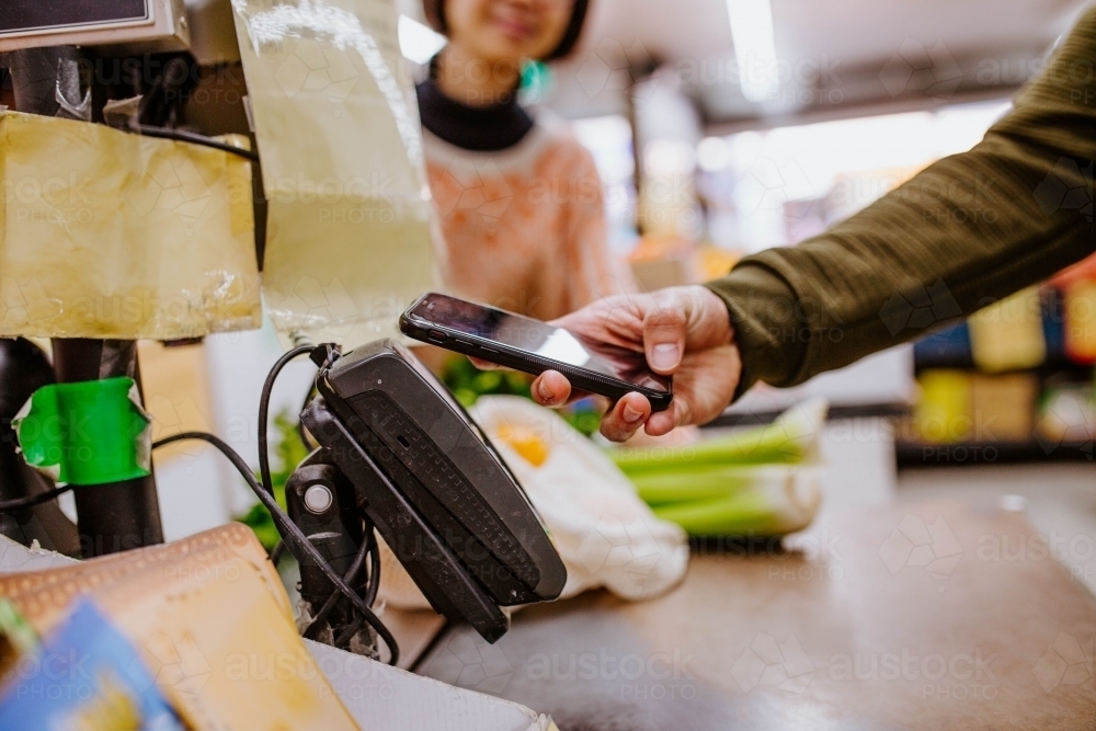 Image of Arm of man paying with phone at supermarket counter - Austockphoto