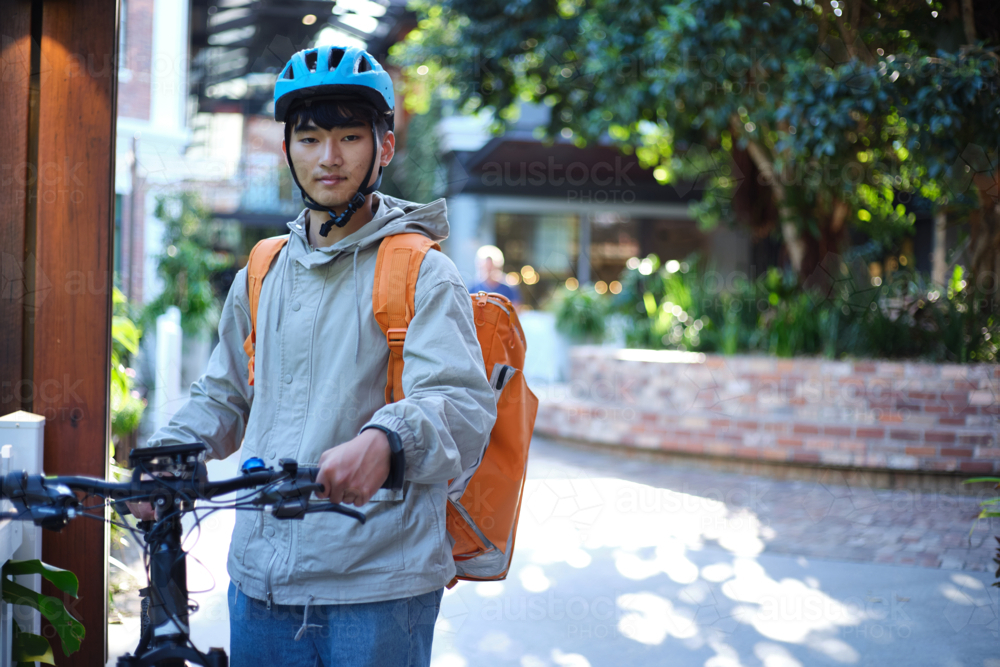 Image of Asian delivery boy walking with his bicycle. - Austockphoto