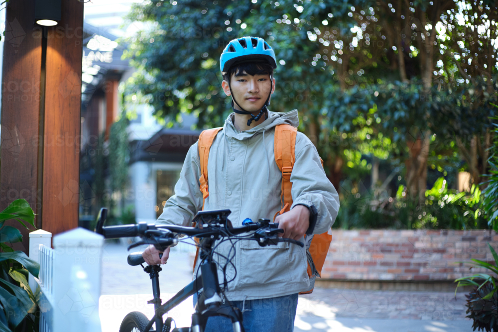 Image of Asian food delivery rider walking with his bicycle - Austockphoto