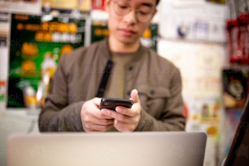 Image of Asian grocery store manager typing on phone - Austockphoto