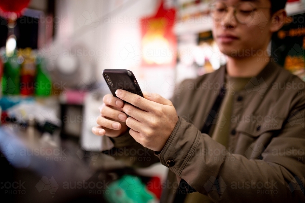 Image of Asian grocery store manager typing on phone - Austockphoto