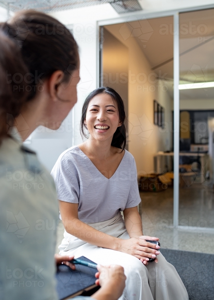 Image of Asian woman smiling while talking to her colleague in an ...