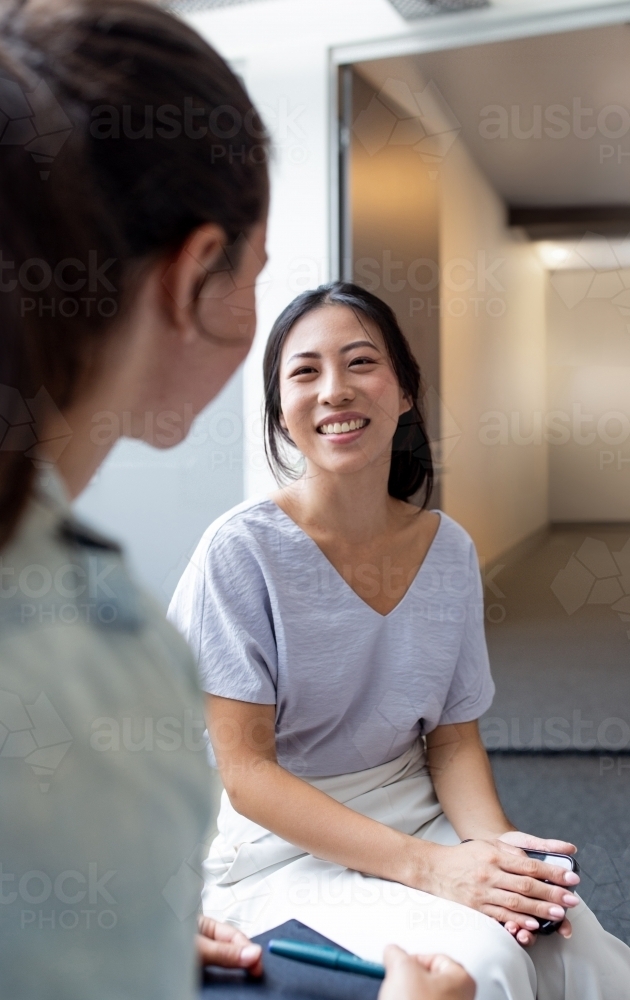 Image of Asian woman smiling while talking to her colleague in an ...