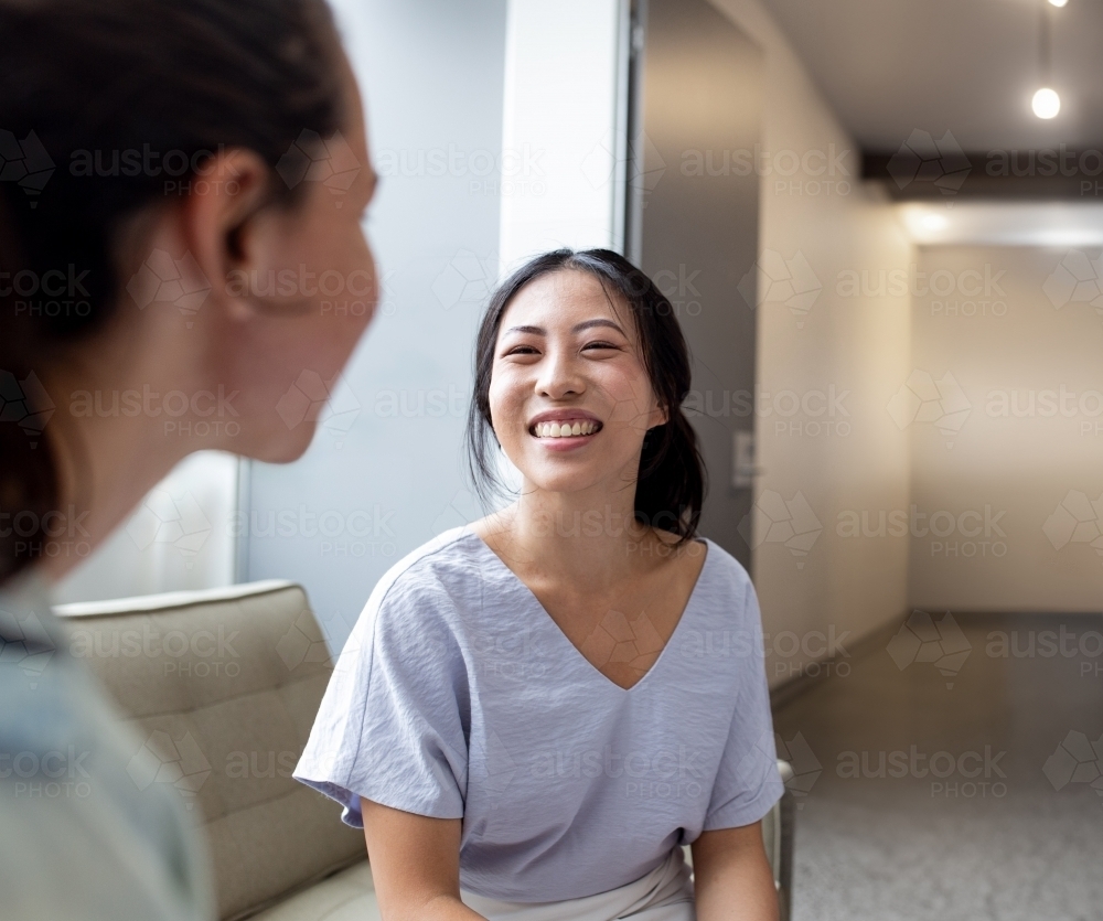 Image of Asian woman smiling while talking to her colleague in an ...