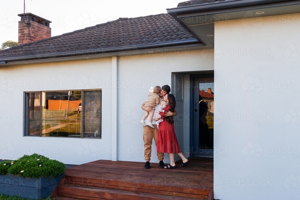 Image of Aussie family of four hug at front door of home - Austockphoto