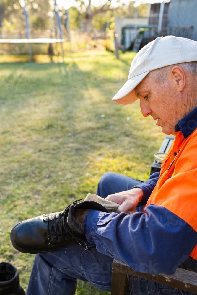 Image of Aussie man in his fifties putting dubbin on work boot ...