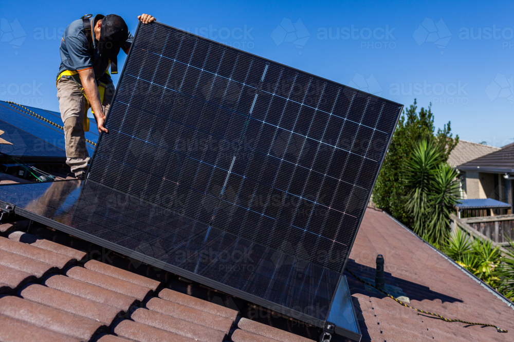 Image of Aussie tradie apprentice helping install solar panels on hot ...