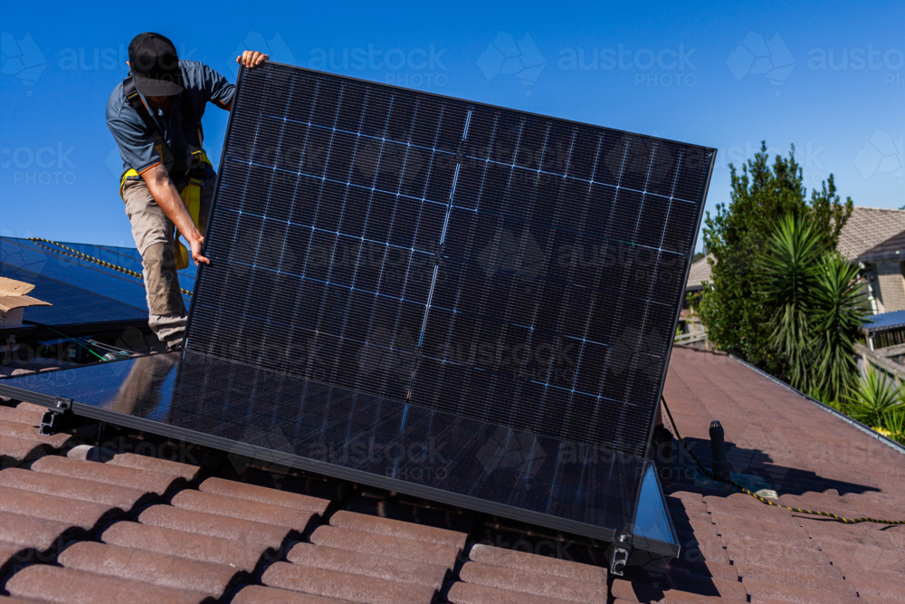 Image of Aussie tradie guy installing solar panels on hot sunlit roof ...