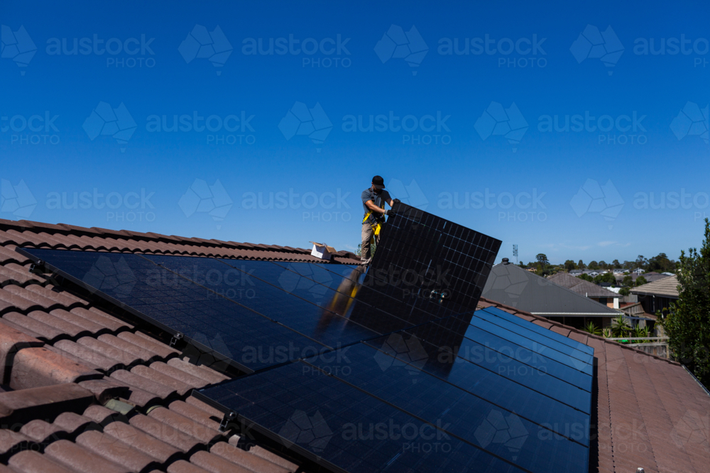 Image of Aussie tradie man installing solar panels on hot sunlit roof ...