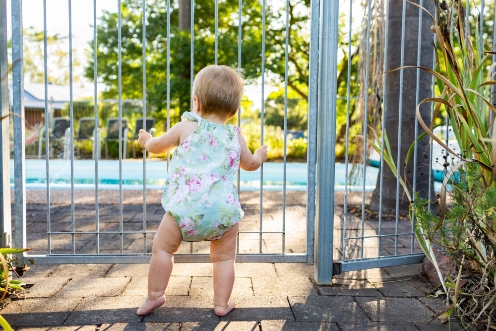 Image of Baby girl at pool gate watching people splashing in the pool ...
