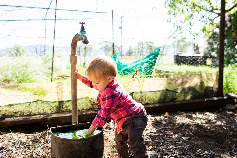 Image of Baby girl on farm playing in animal water in chook yard ...