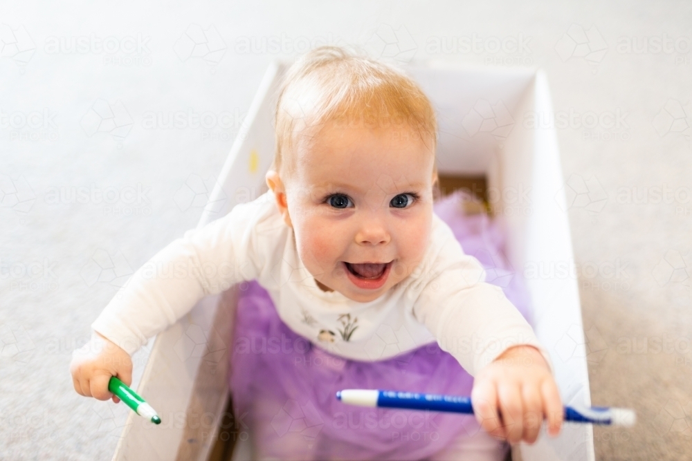 Image of Baby girl sitting in box drawing with crayon textas at home ...