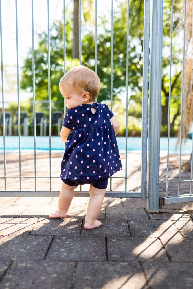 Image of baby girl standing at backyard pool gate fence - Austockphoto