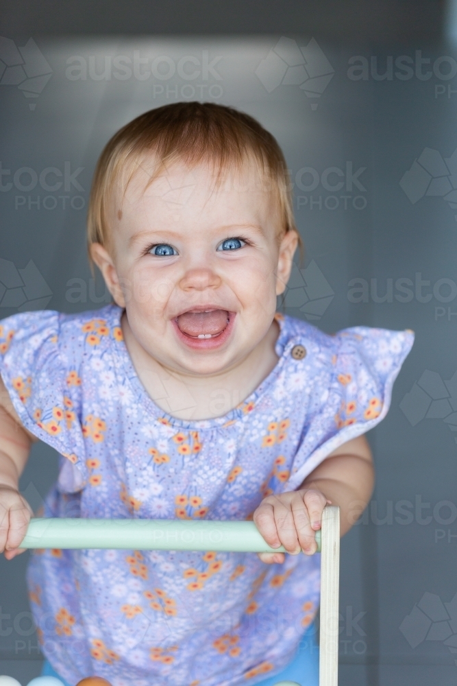 Image of Baby girl with big smile walking with push walker - Austockphoto