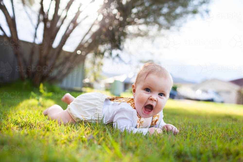 Image of Baby lying on tummy on front lawn of suburban home yawing ...