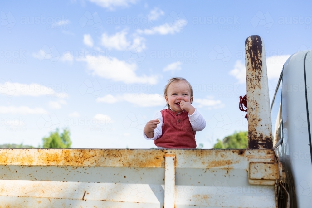 Image of Baby on back of farm ute with copy space and blue sky behind ...