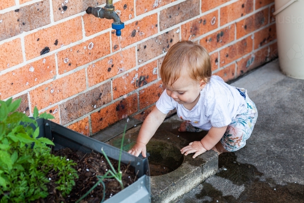 Image of Baby playing with water and tap drain splashing in backyard ...