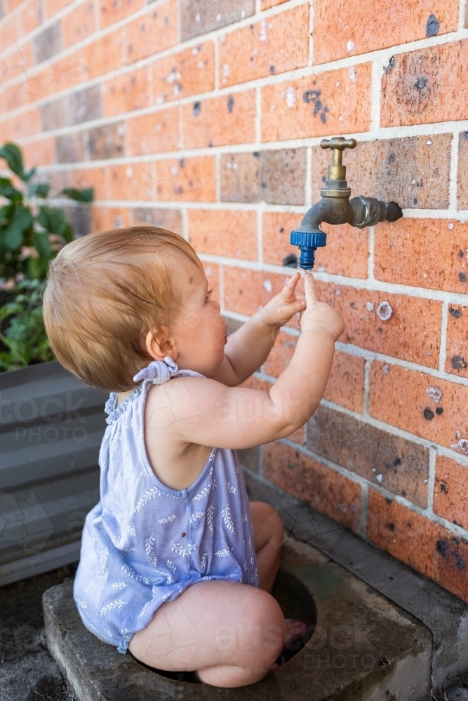 Image of baby putting fingers in tap in backyard, messy water play ...