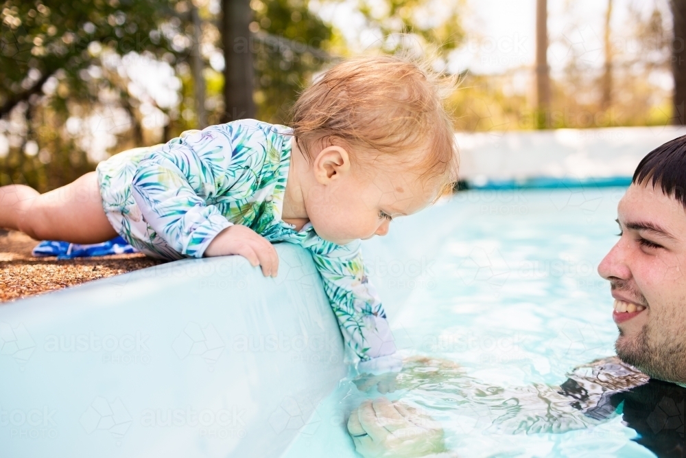 Image of Baby reaching into swimming pool being supervised by parent ...
