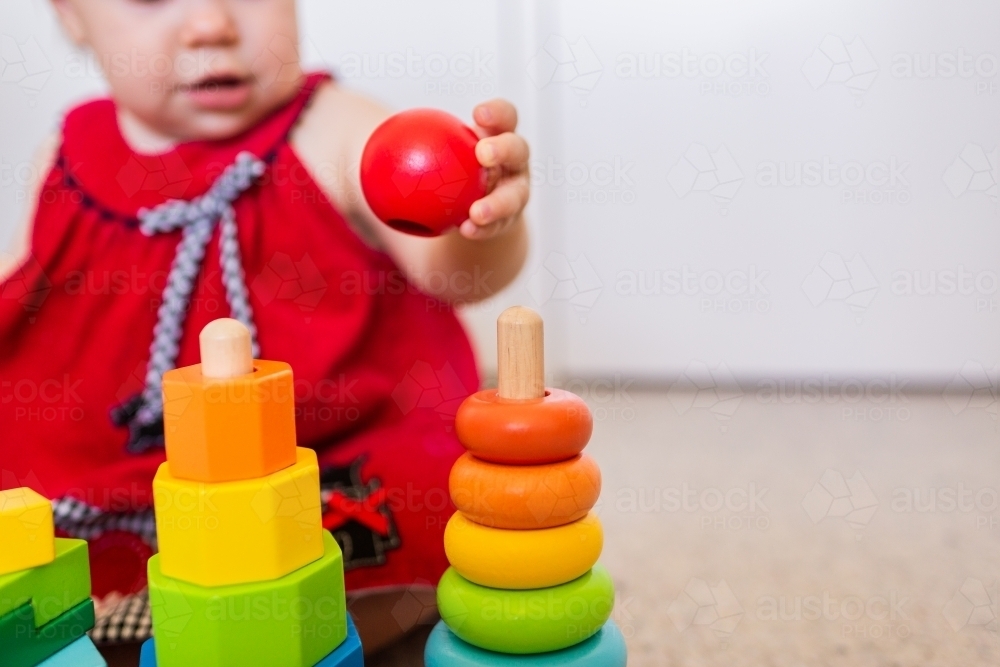 Image of Baby sitting on floor playing with colourful stacking fine ...