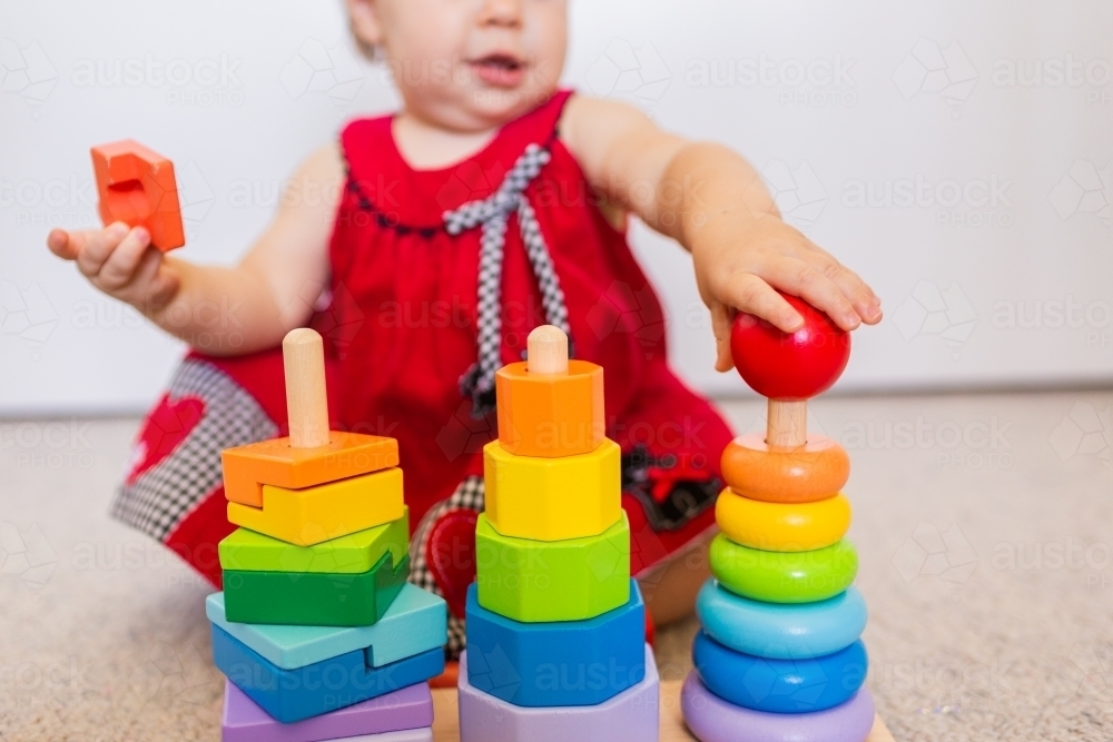 Image of Baby sitting on floor playing with colourful stacking fine ...