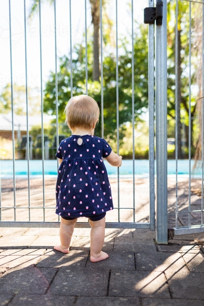 Image of Baby standing at closed inground pool fence gate in backyard ...