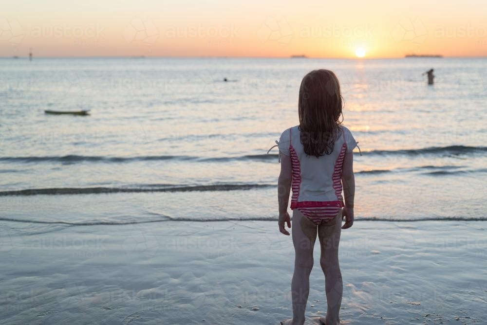 Image Of Back View Of A Lone Young Girl Standing On The Beach Watching The Sunset Over The Ocean