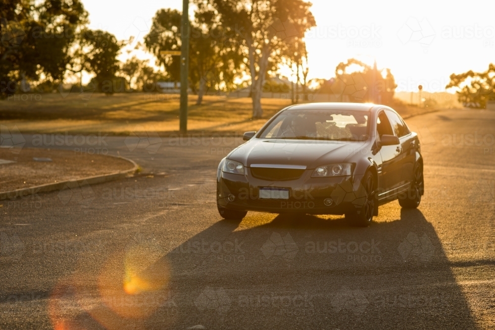 Image of backlit photo of sedan car driving down quiet street in ...