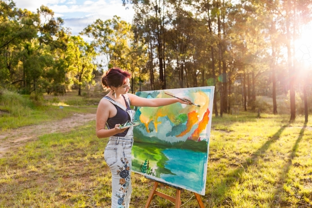 Image of Backlit young artist in forest clearing working on large ...